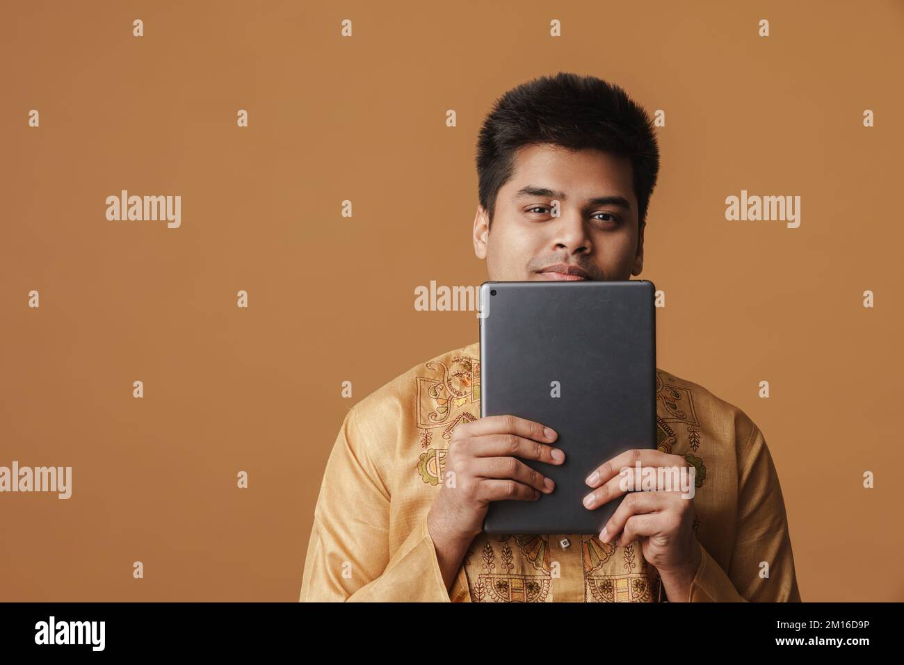 Young brunette indian man smiling and holding tablet computer isolated ...