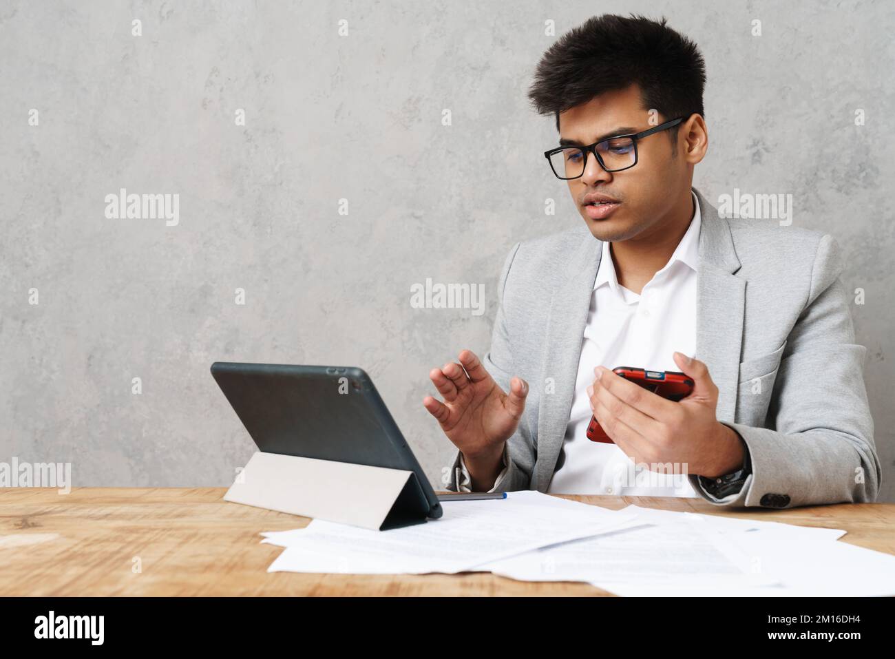 Young serious indian businessman using tablet computer and cellphone ...