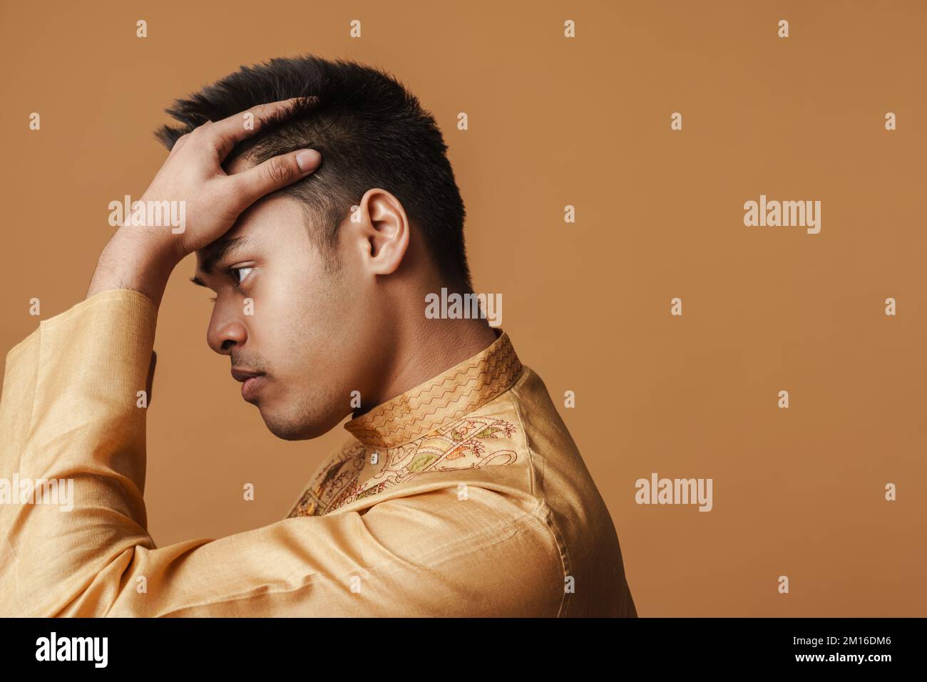 Young brunette indian man standing in profile and touching his head ...