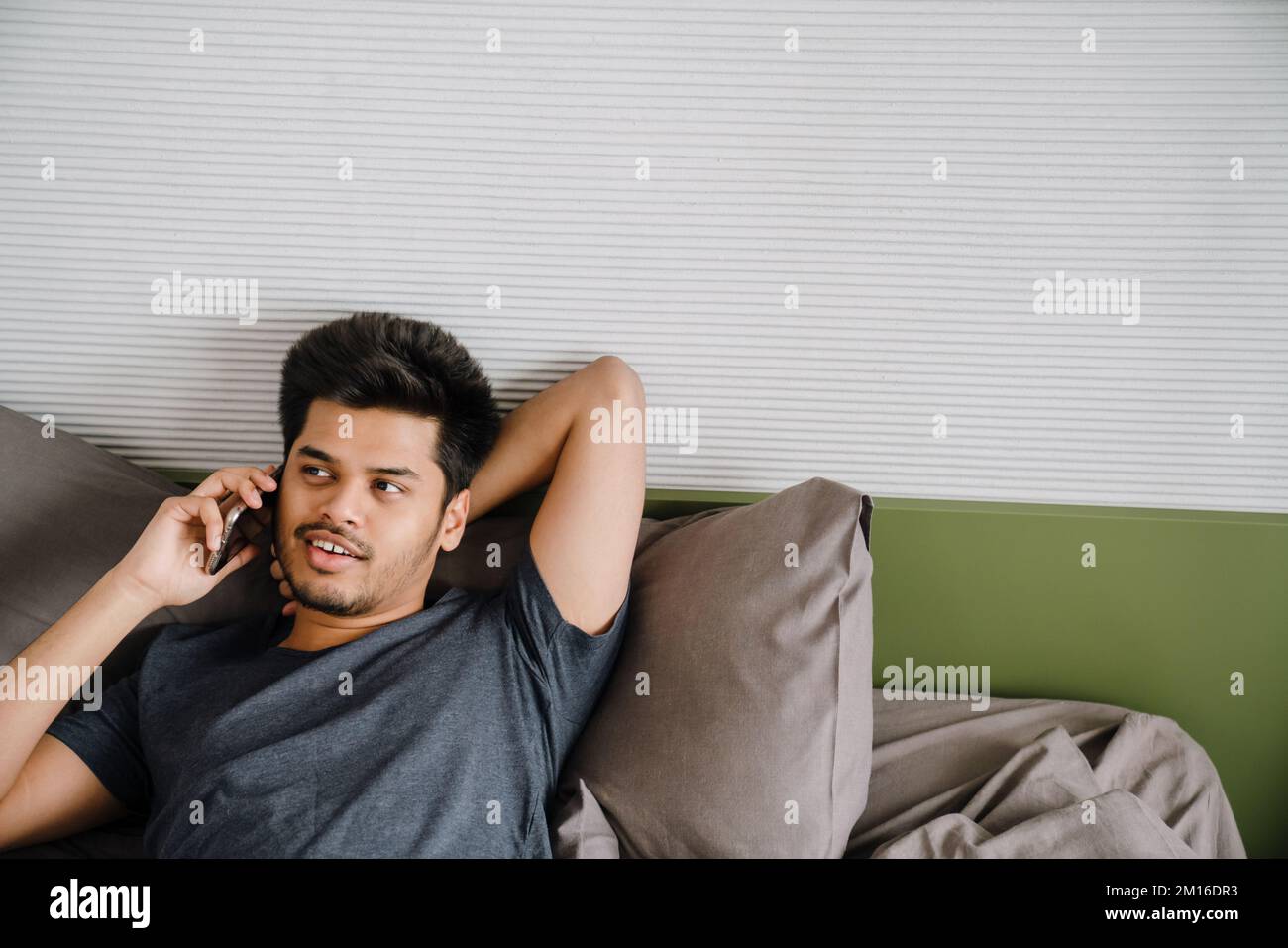Young indian man liying on bed with hand behind his head and talking ...