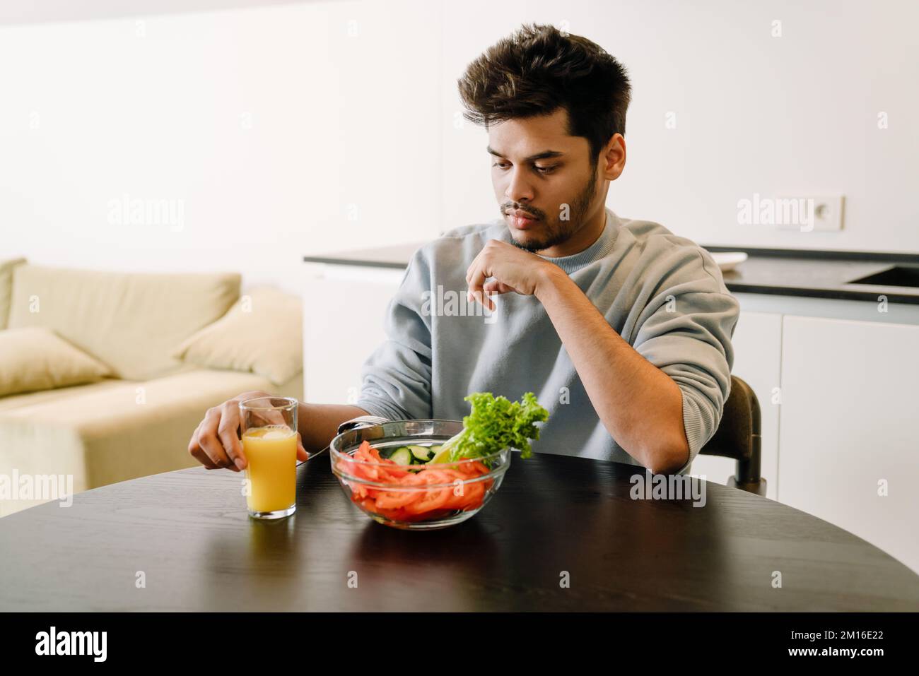 Young indian man with orange juice and fresh salad sitting on kitchen ...