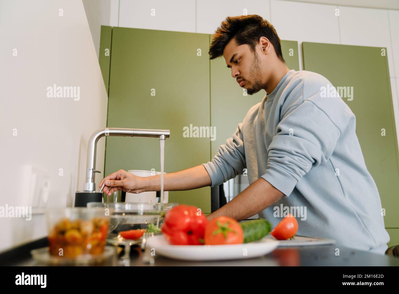 Adult indian man washing vegetables to cook salad in cozy kitchen at ...
