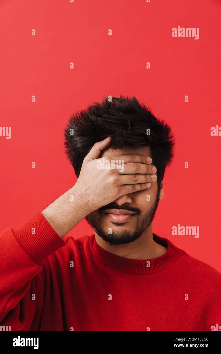 Young brunette indian man smiling and covering his eyes isolated over ...