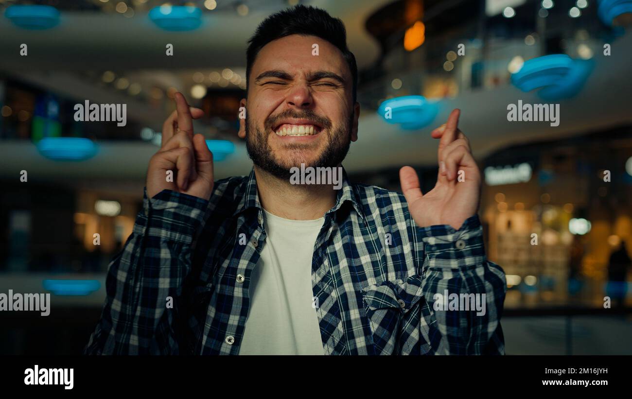 Hopeful man stand in shopping mall praying crosses fingers for hope ...