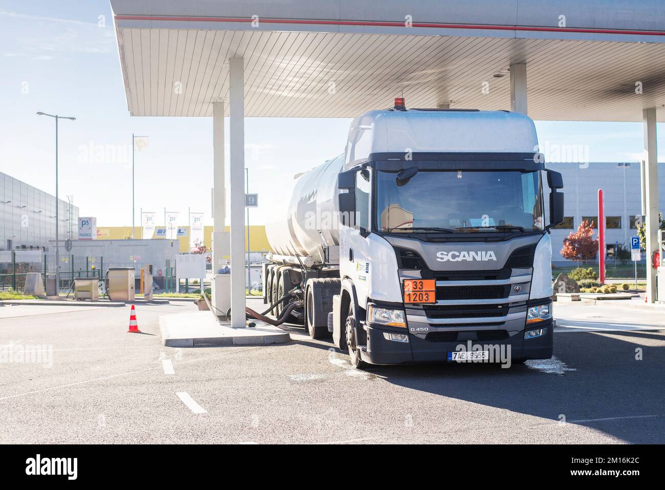 A white fuel tanker truck at a petrol station connected by a hose to ...