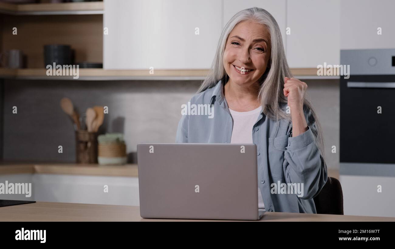 Happy middle aged senior grandma sit at home use laptop check email ...