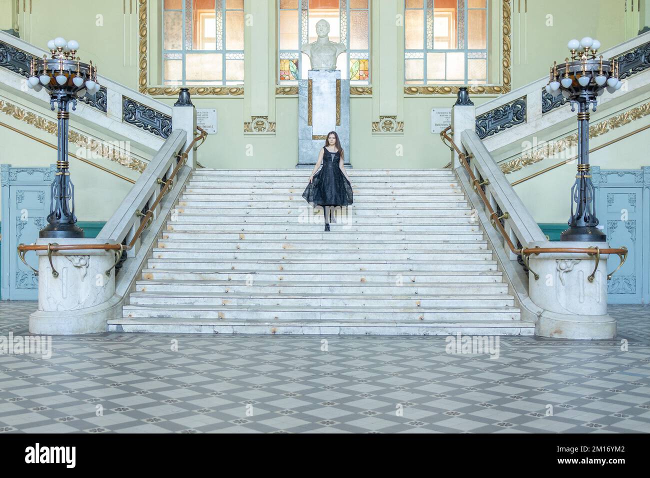 Beautiful girl in black dress running down wide stairs in hall ...