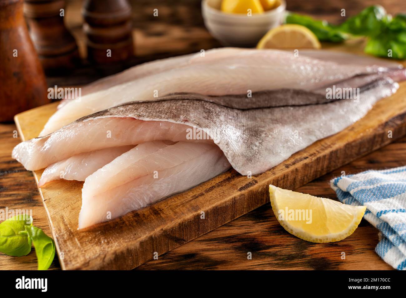 Fresh haddock fillets on a rustic cutting board with lemon and herbs ...