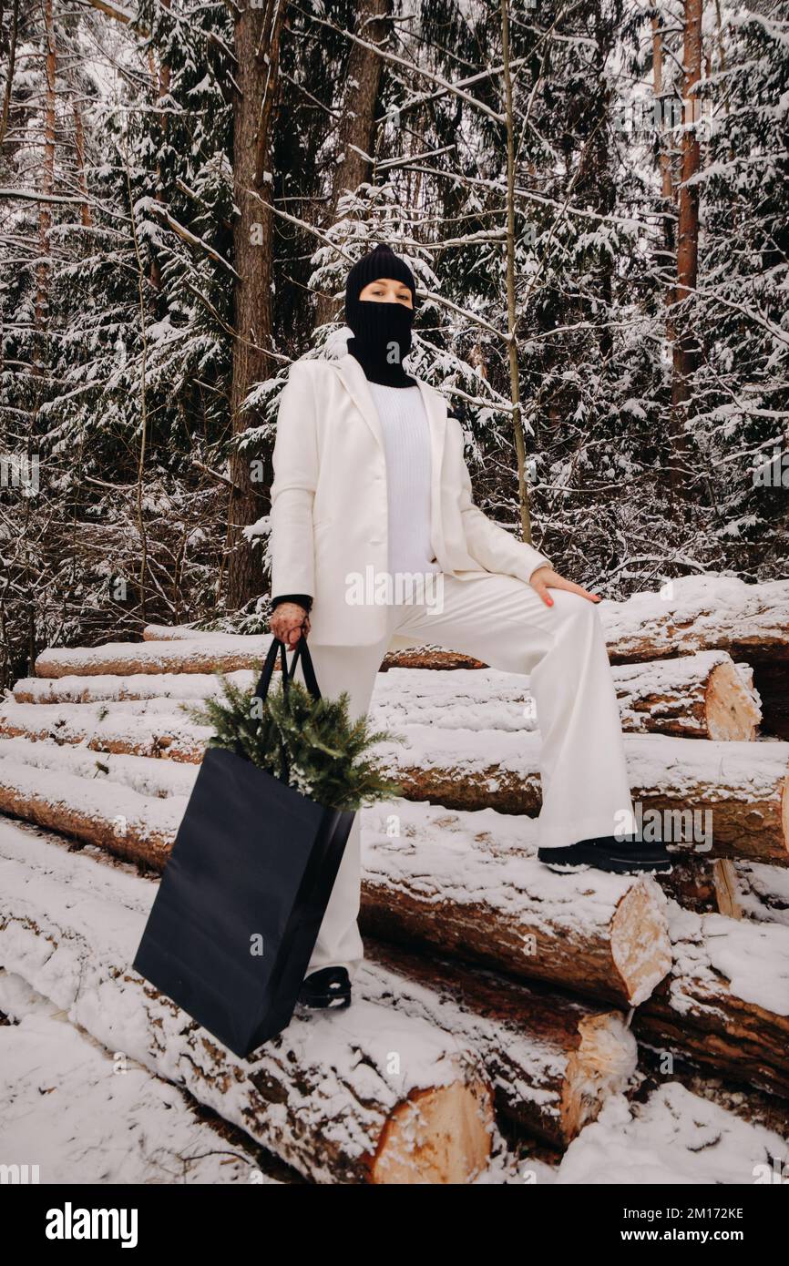 A girl in a white suit and balaclava with a package of Christmas trees ...
