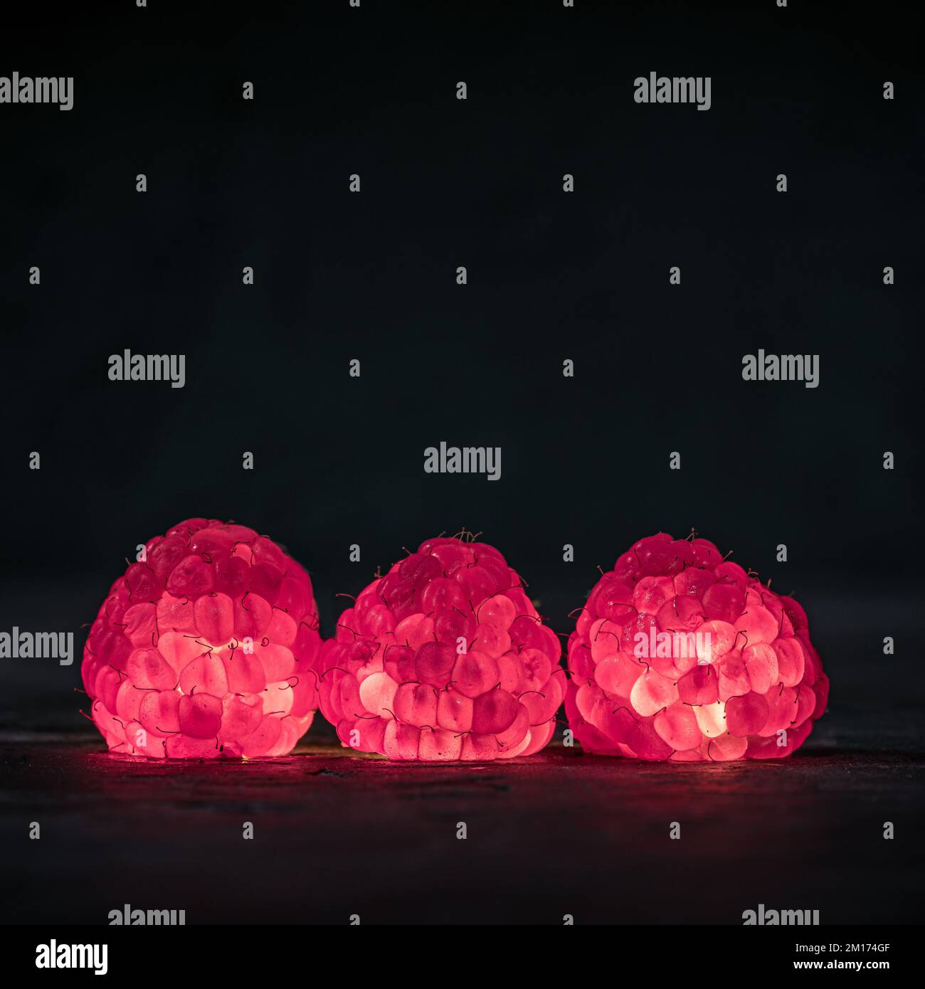 Three isolated illuminated raspberry on dark slate background. view ...