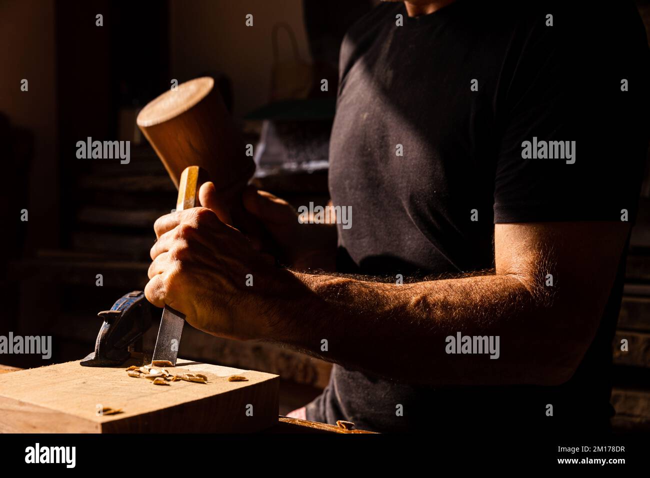 A close up of man's hands using a chisel and a mallet on a piece of ...