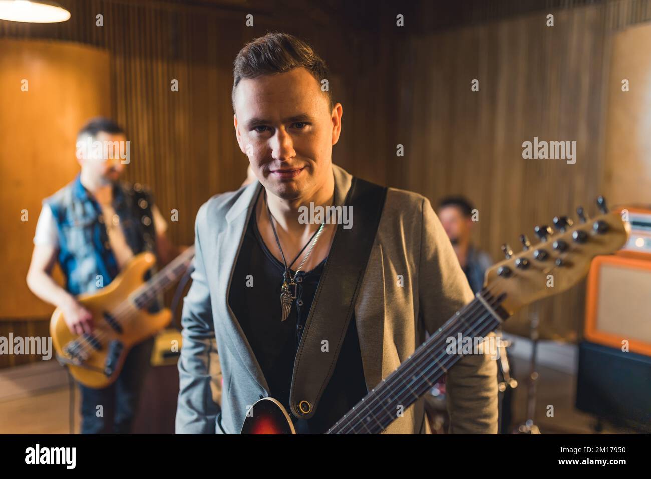 medium shot of a young Caucasian guitarist posing and other musicians ...