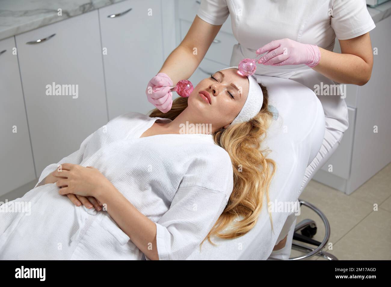 Young woman receiving facial massage with glass balls in beauty salon ...