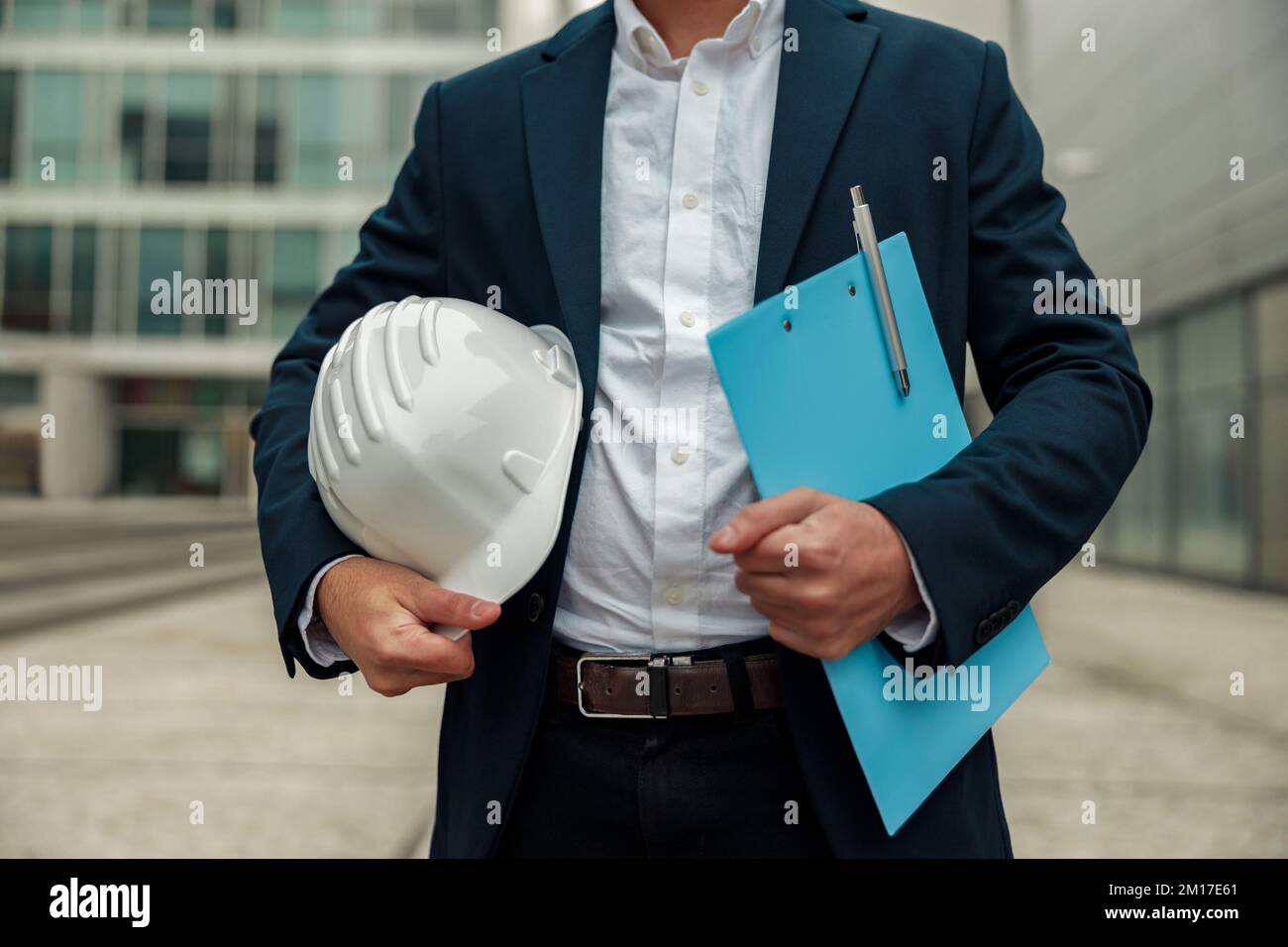 Close up of engineer in suit holding protective helmet and paper folder ...