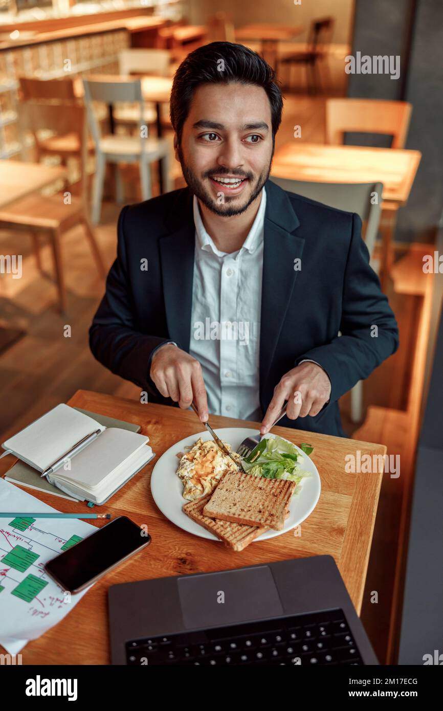 Indian businessman eating lunch during break after work in cafe and looking at side Stock Photo ...