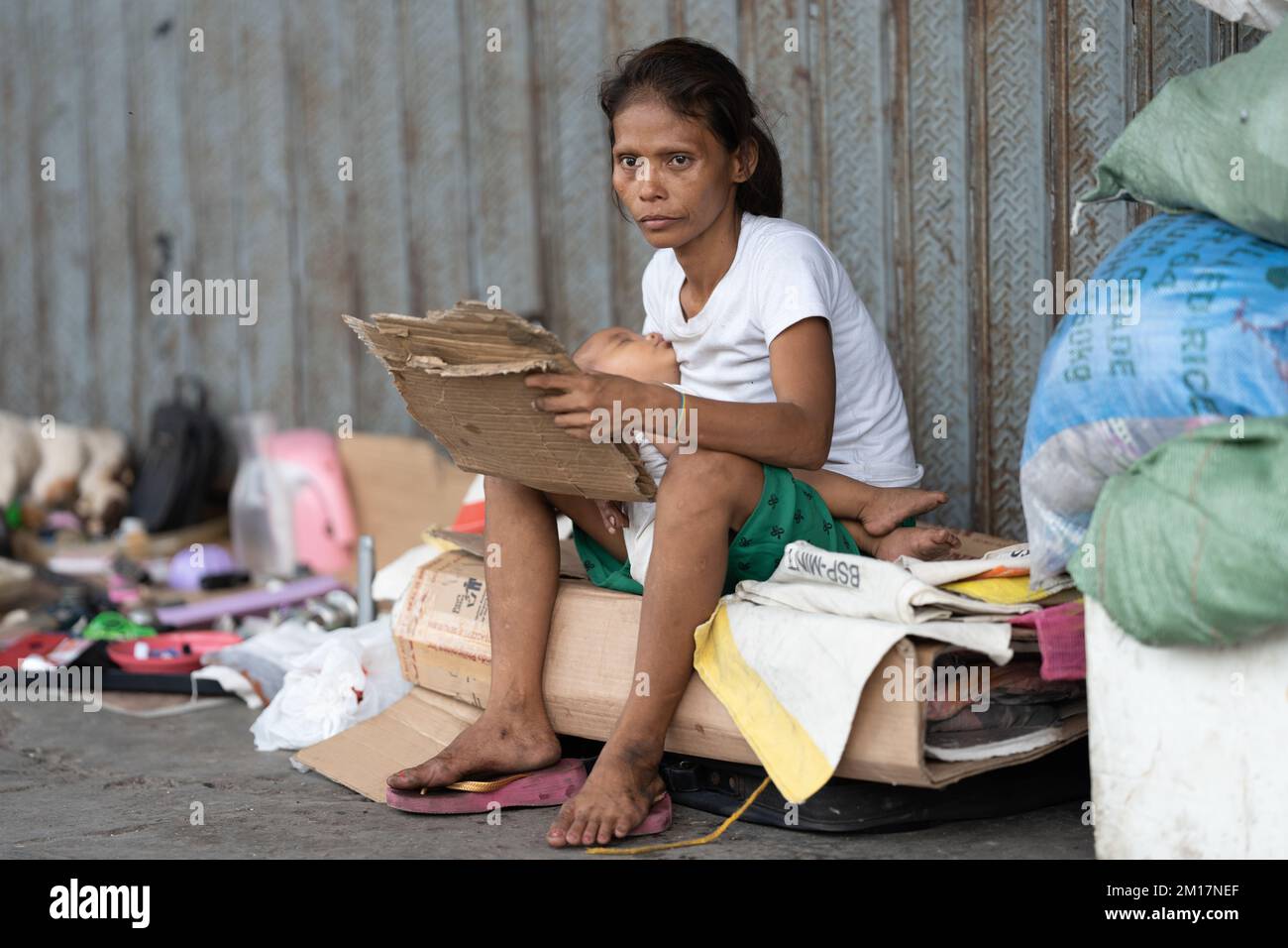A homeless woman sits with her child on a makeshift bed made of ...