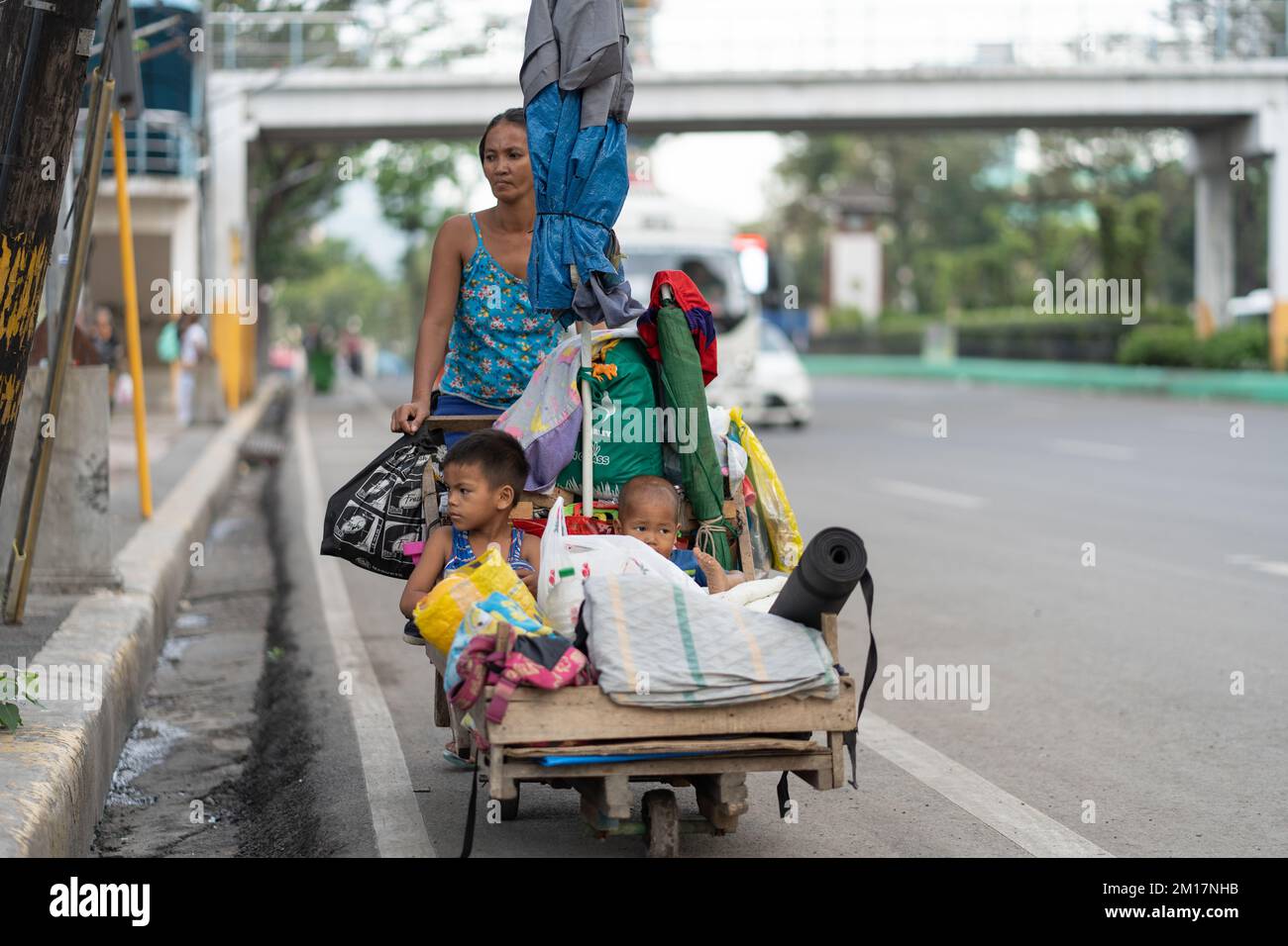 A Homeless Woman Pushing A Cart With Her Belongings And Two Small