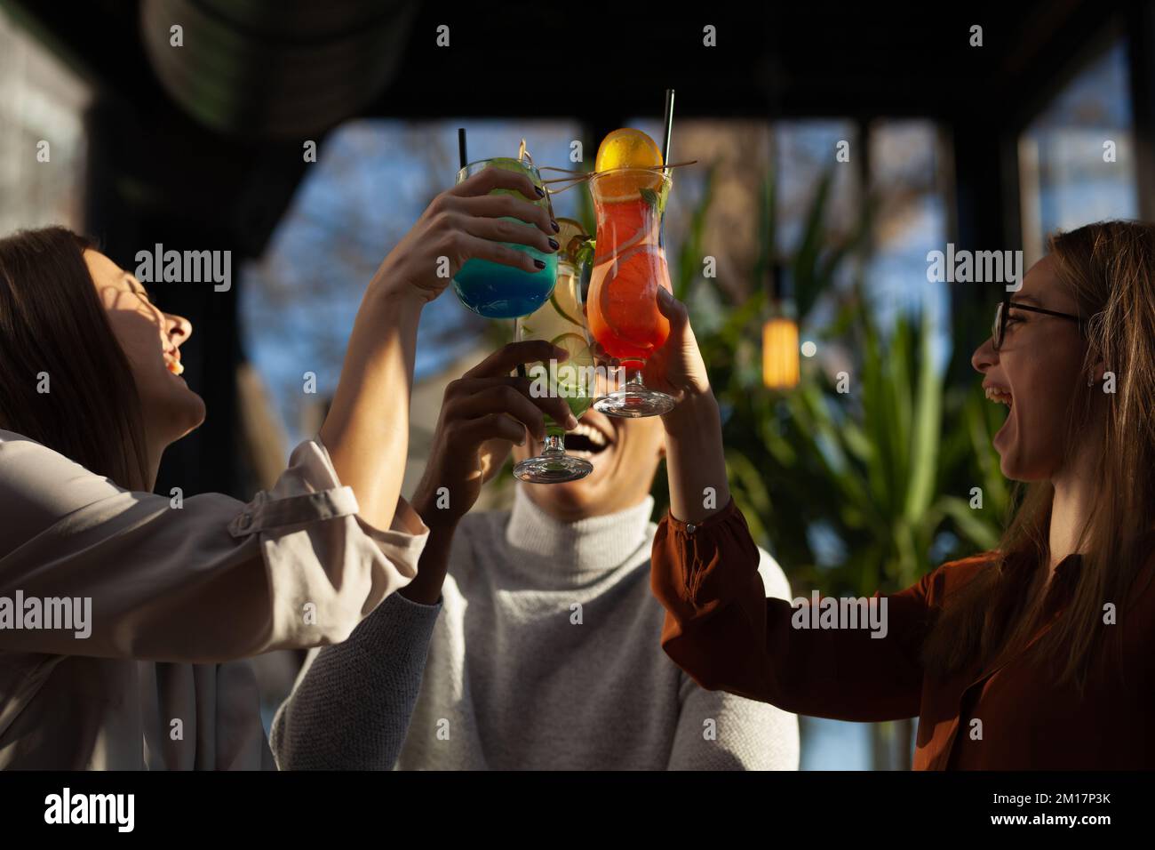 Three multiracial friends in a bar cheering. After work party with ...