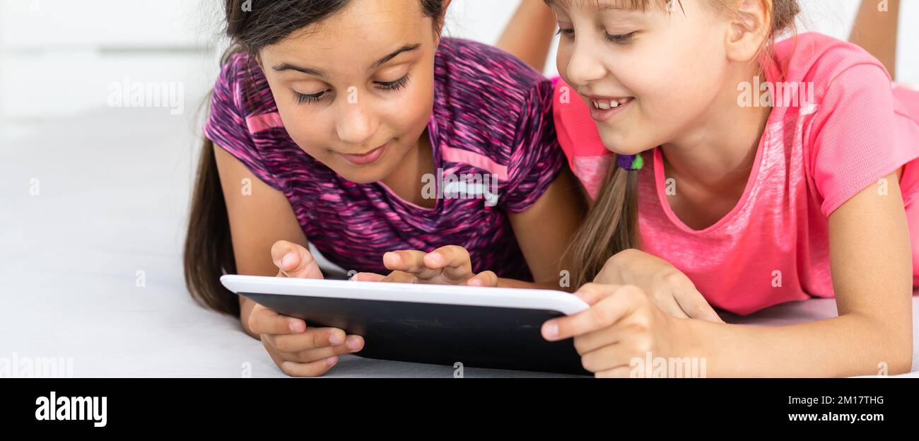 Two cute little girls are using a digital tablet and smiling while ...