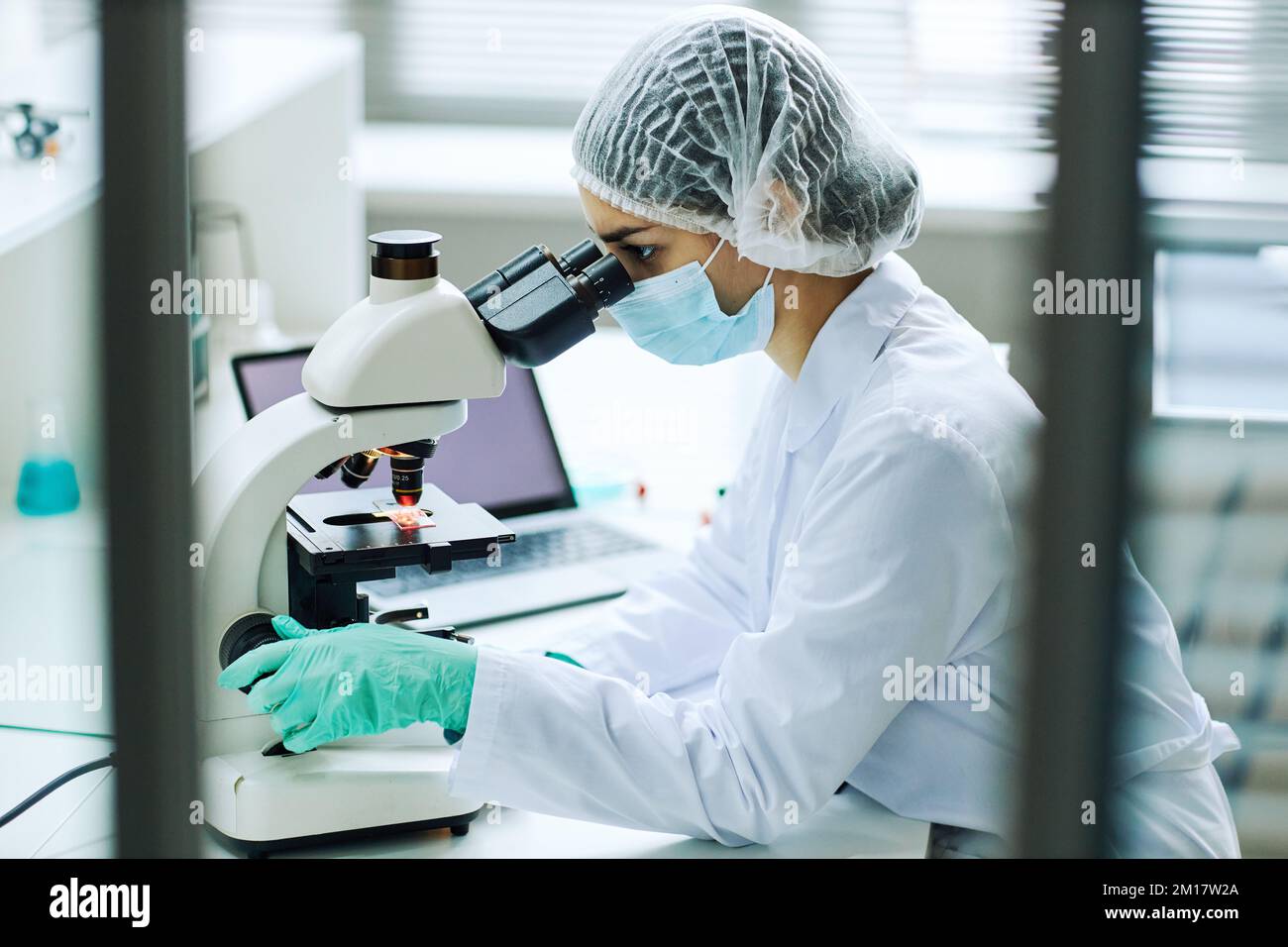 Side view portrait of young female technician looking in microscope ...