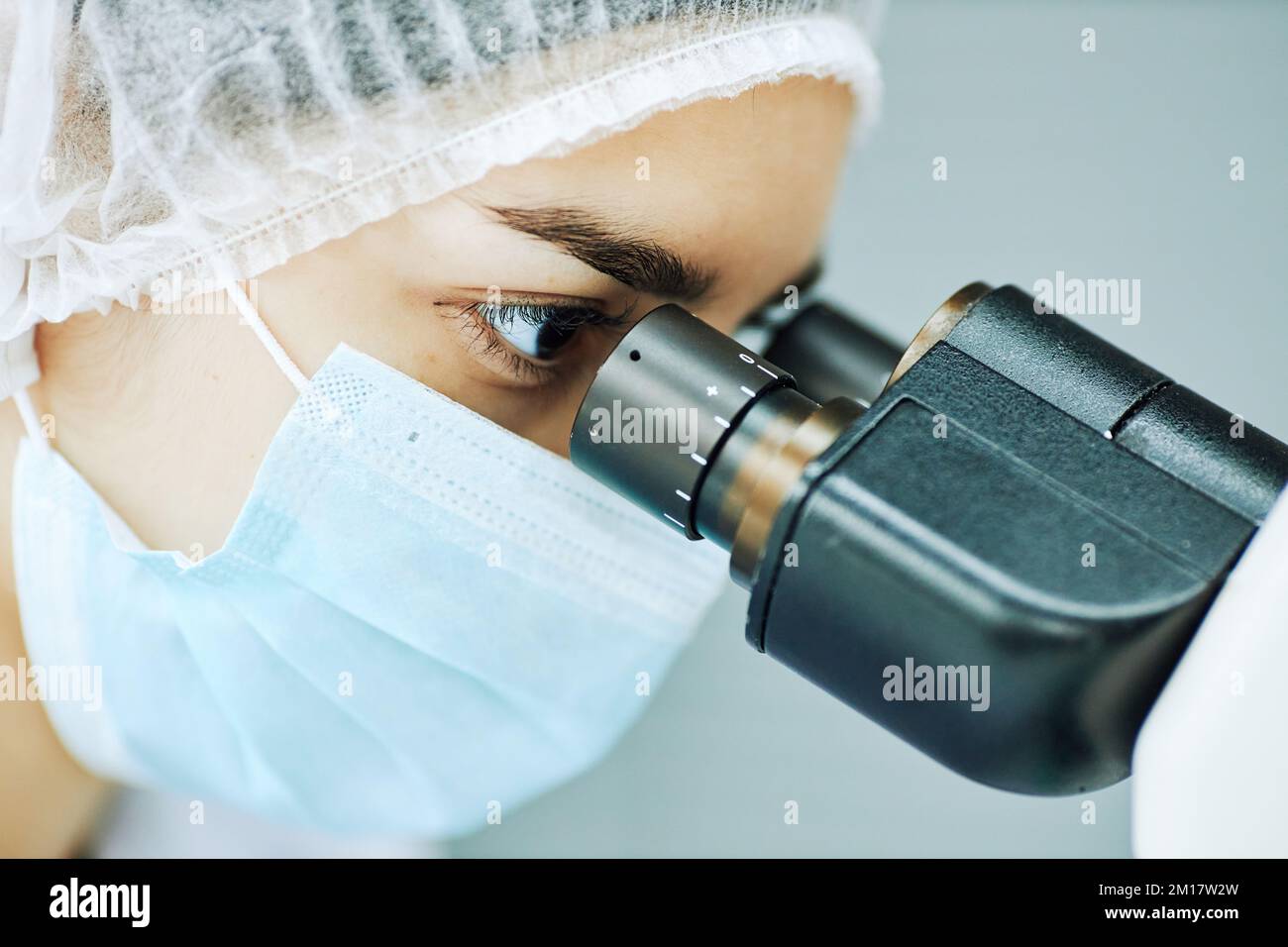 Side view closeup of young female medic looking in microscope while ...