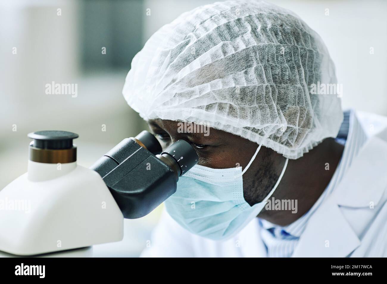 Side view portrait of black scientist looking in microscope while ...