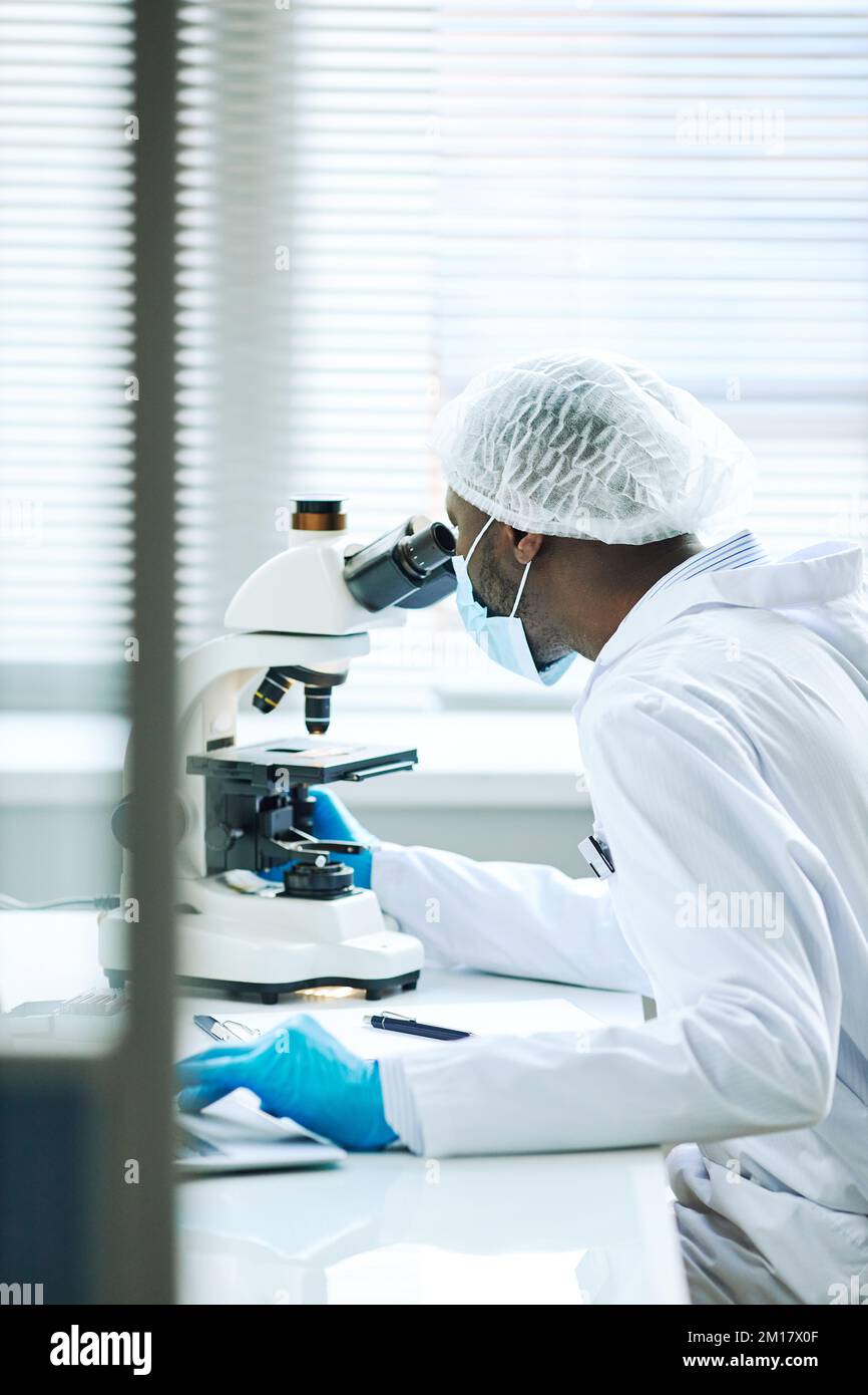 Vertical portrait of male scientist using microscope in medical lab ...