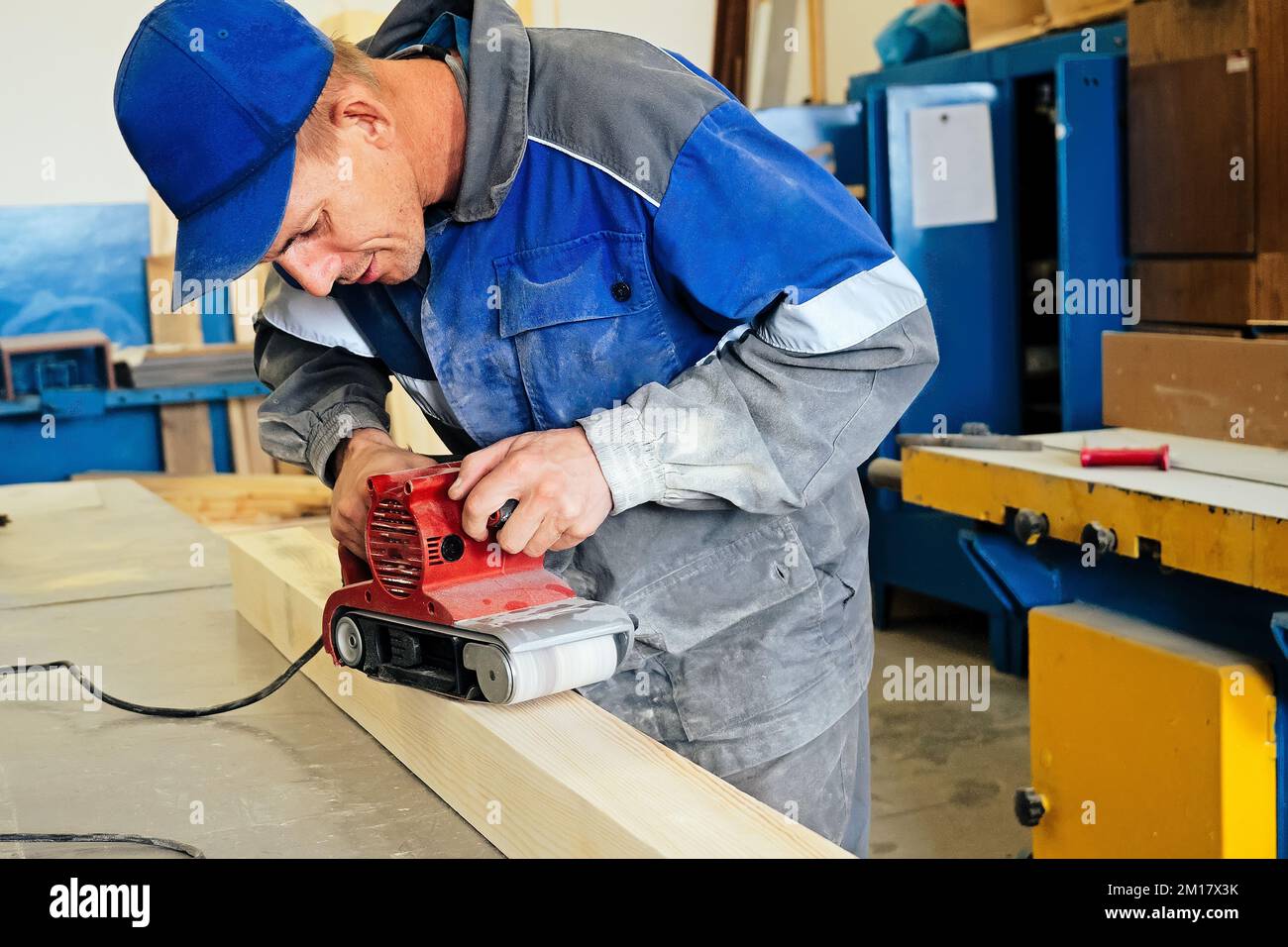 Carpenter in work clothes processes wood with grinder. Polishing of ...