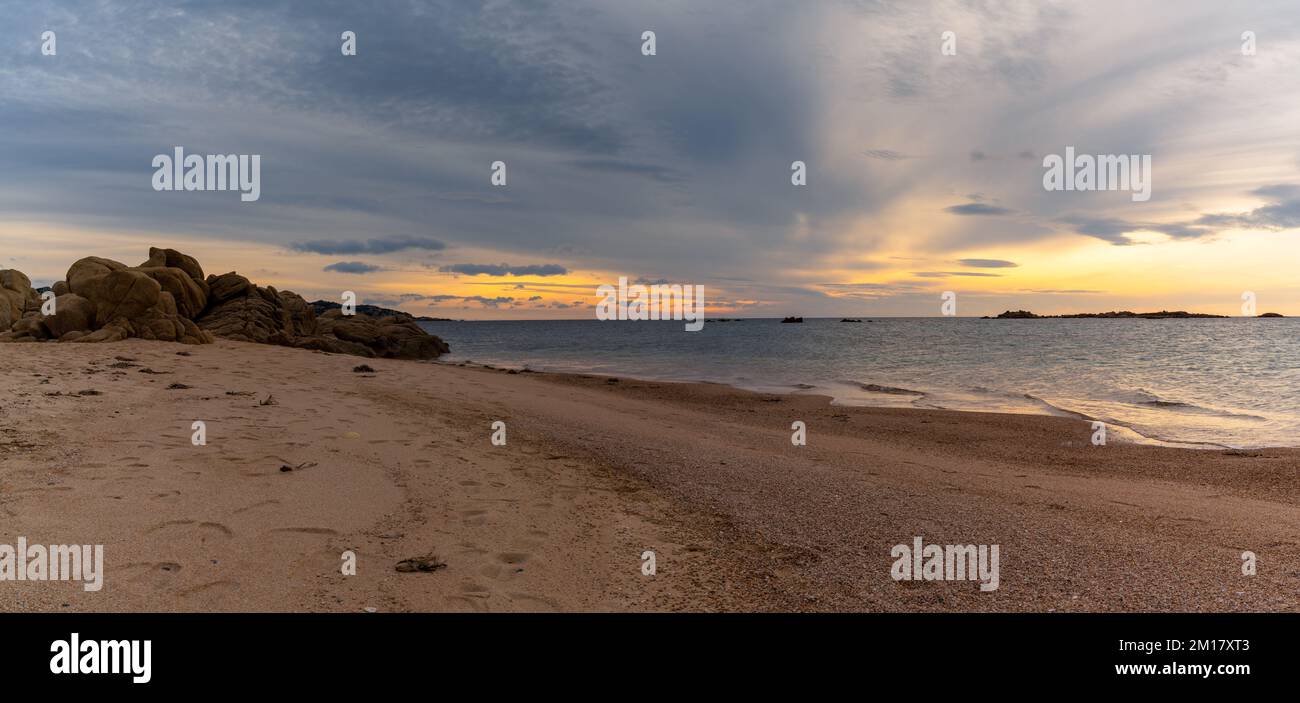 A panorama view of a golden sand beach at sunset with calm ocean water ...