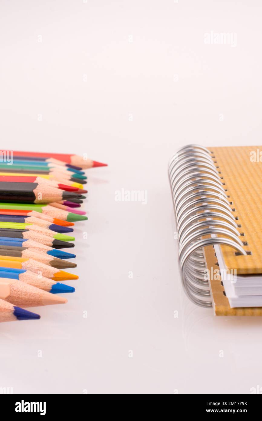 Color pencils of various colors near a notebook on a white background ...