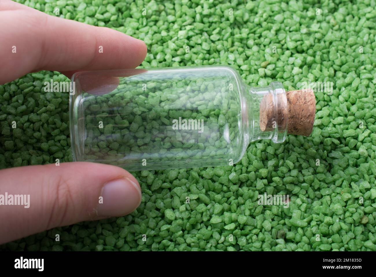 Empty little bottle in hand on green sand Stock Photo - Alamy