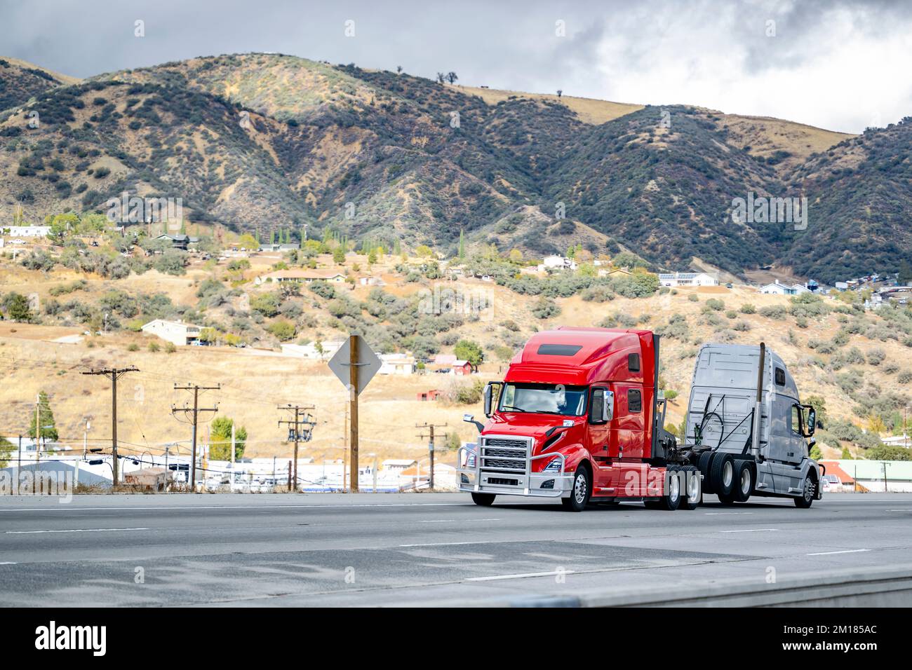 Bright red big rig semi truck tractor towing another team semi truck ...