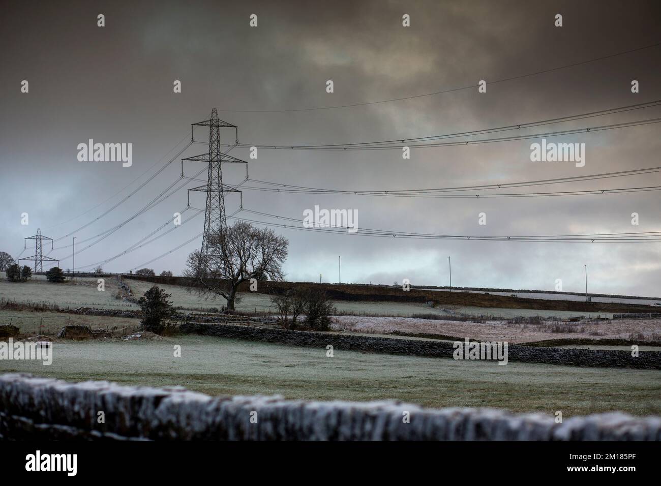 Pylons covered in frost and light snow cross West Yorkshire farm fields ...
