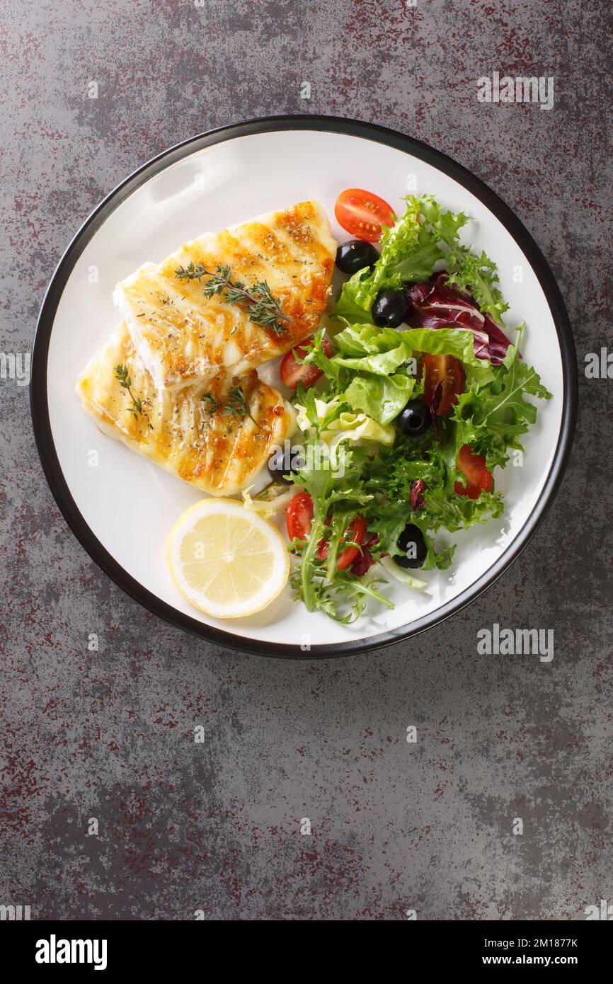 Grilled cod with fresh salad tomatoes, olives, lettuce mix close-up in ...