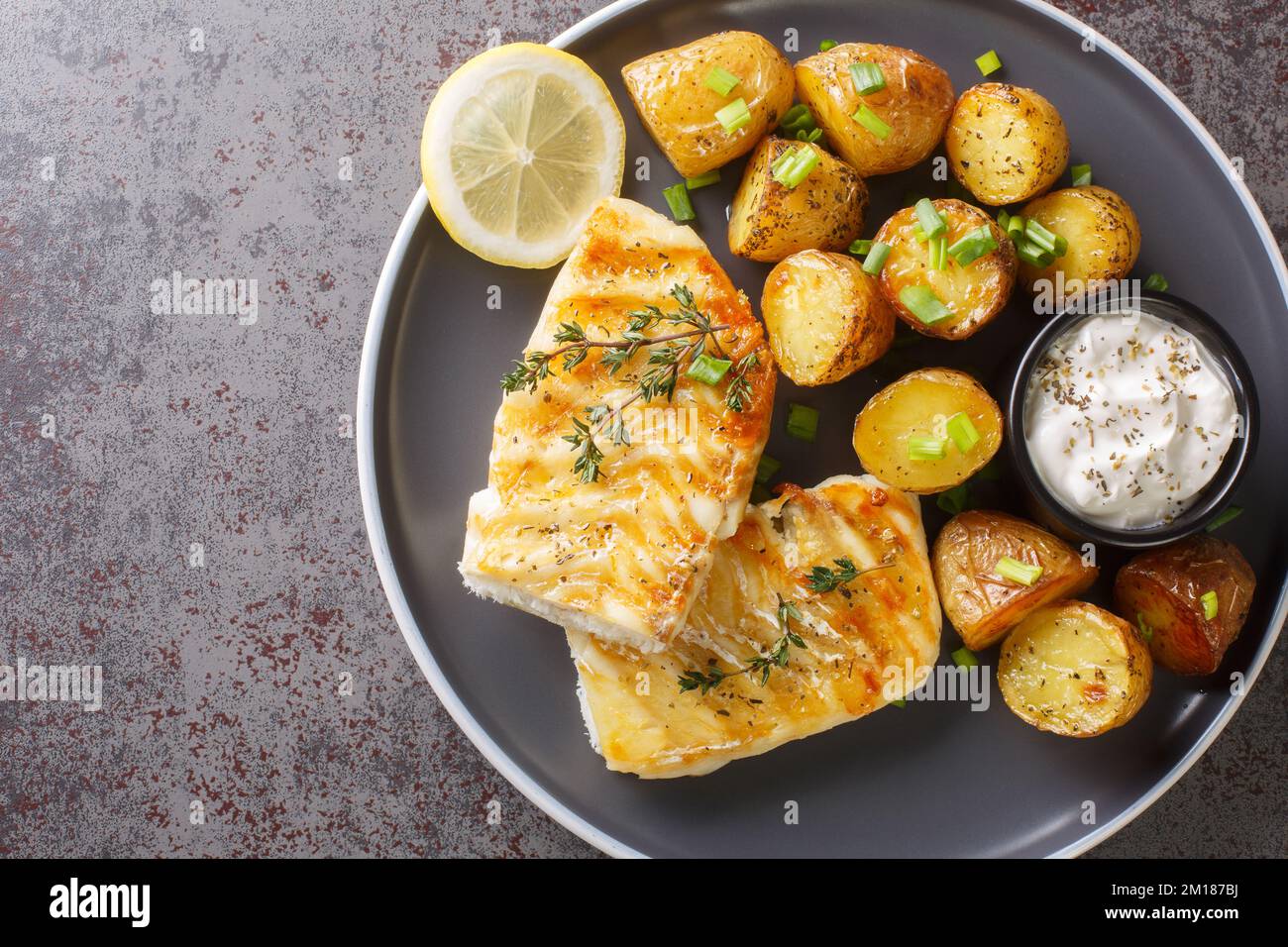 Portion of grilled cod fish with baked jacket potatoes, creamy sauce ...