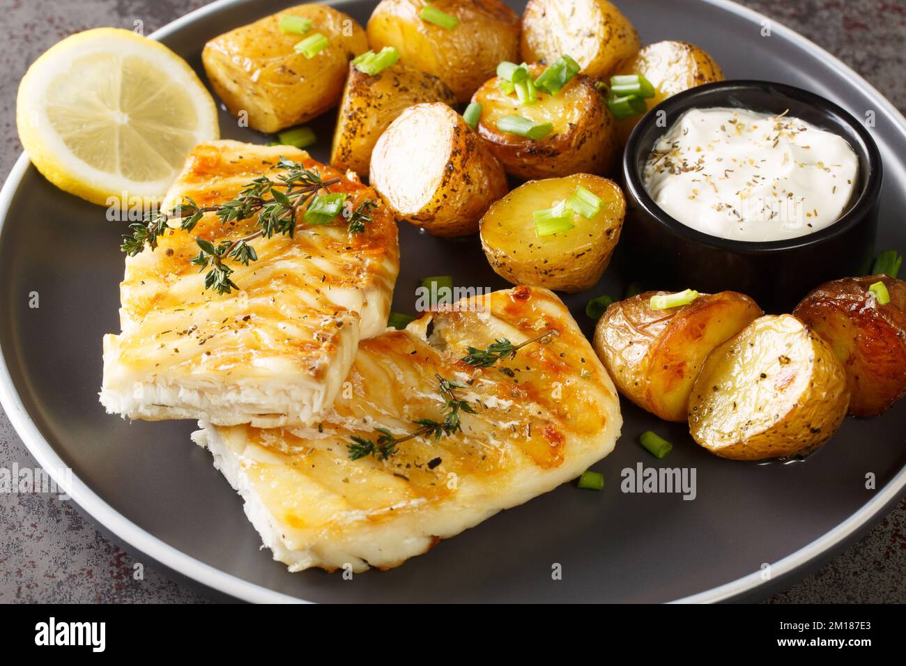 Portion of grilled cod fish with baked jacket potatoes, creamy sauce ...