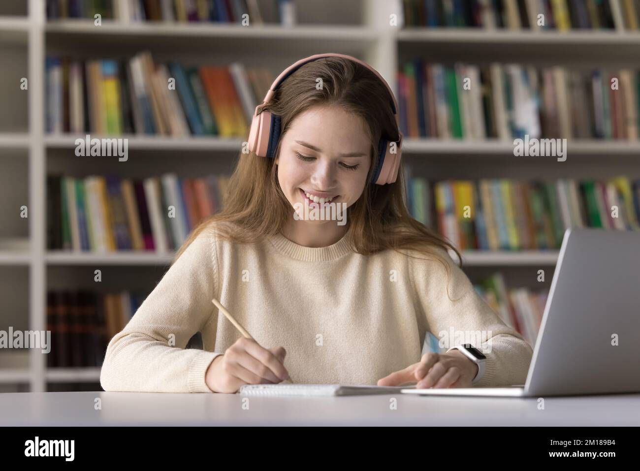 Cheerful student girl in bog wireless headphones watching learning ...