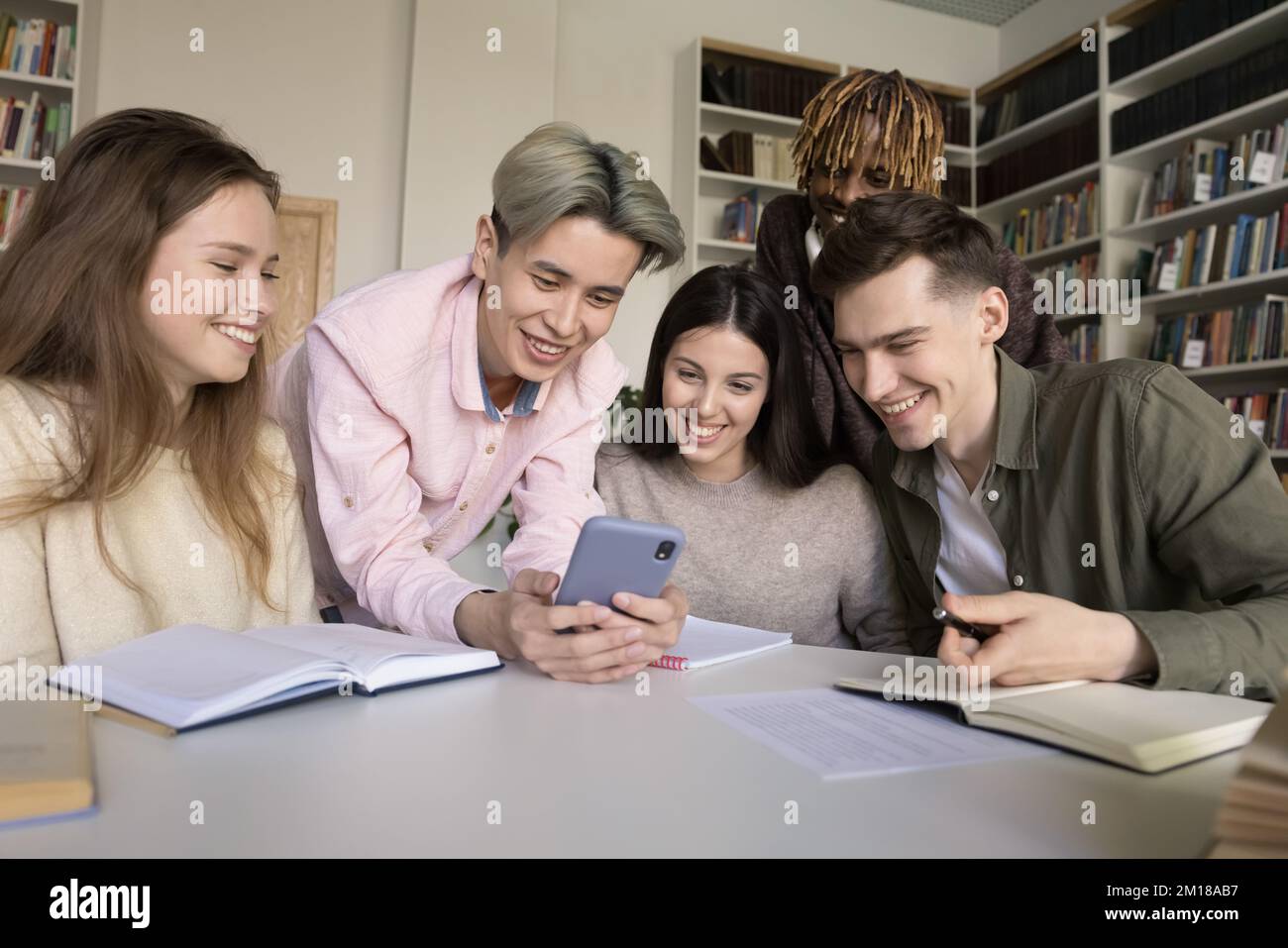 Diverse team of cheerful teenager students using smartphone together ...