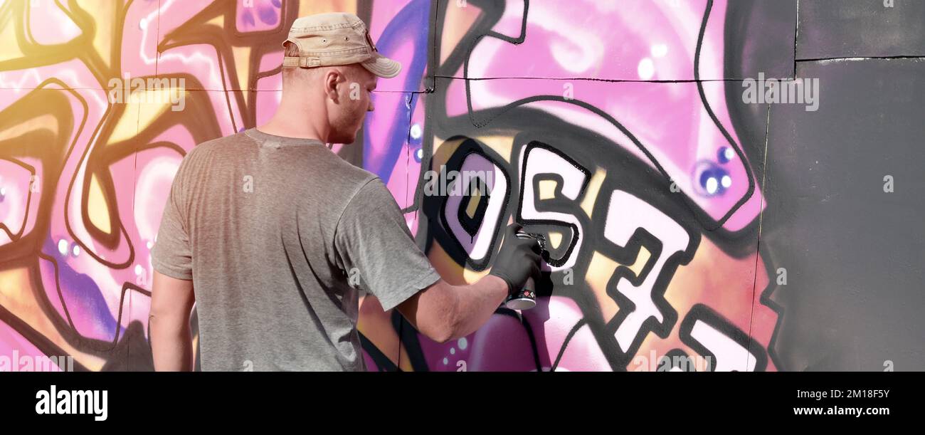 Young caucasian male graffiti artist drawing big street art painting in ...