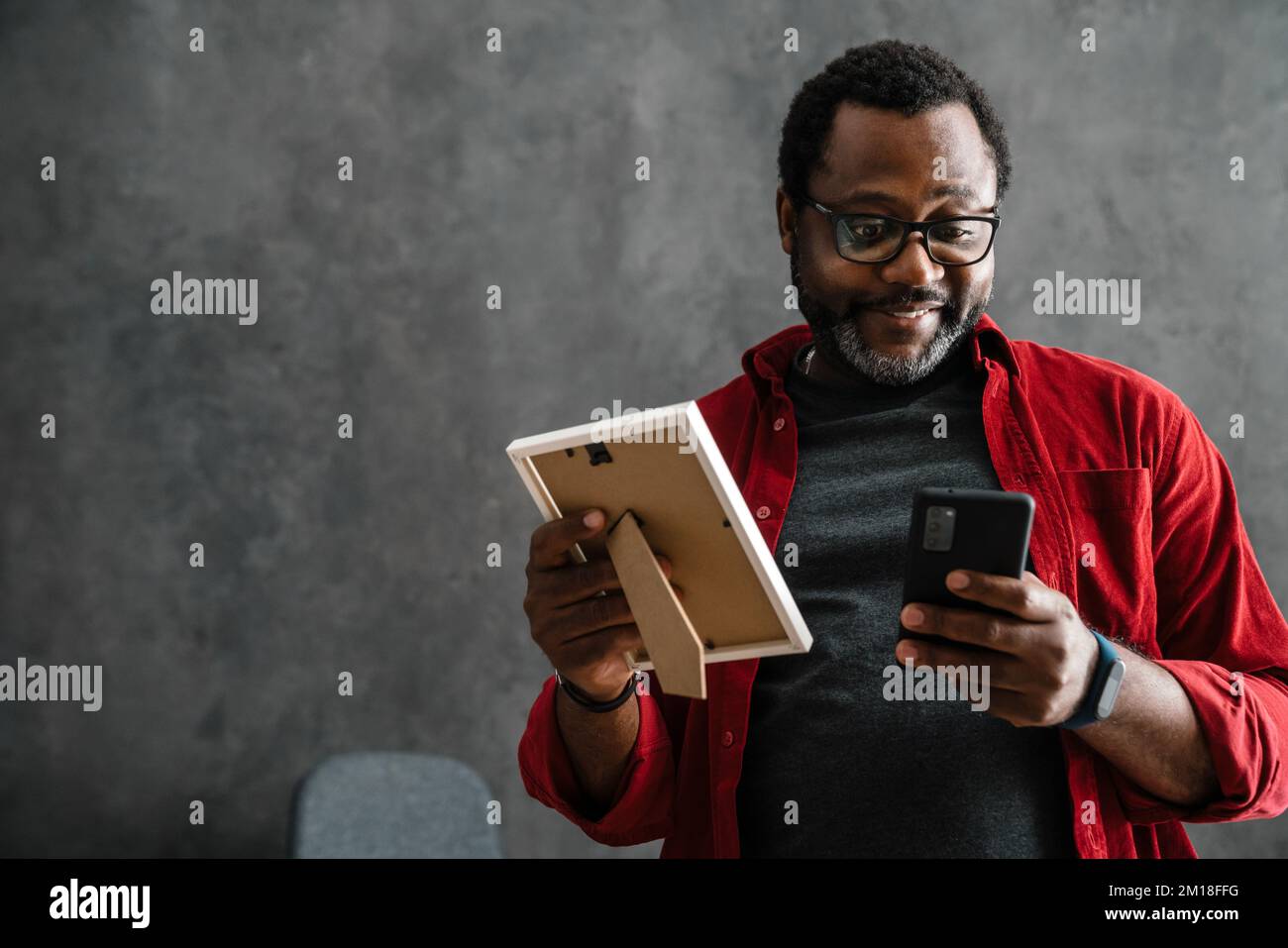 Black man using mobile phone and holding photo frame while working in ...
