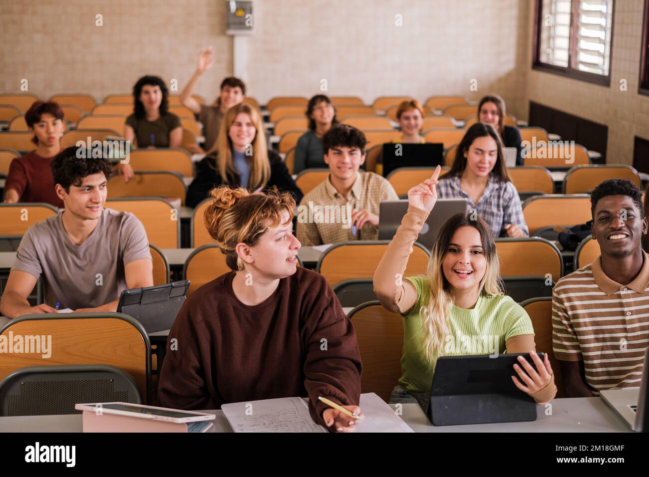 Group of college students raising their hands to ask the teacher during ...