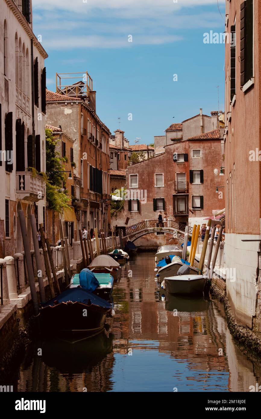 A small side channel with boats, red buildings, and a small bridge in ...