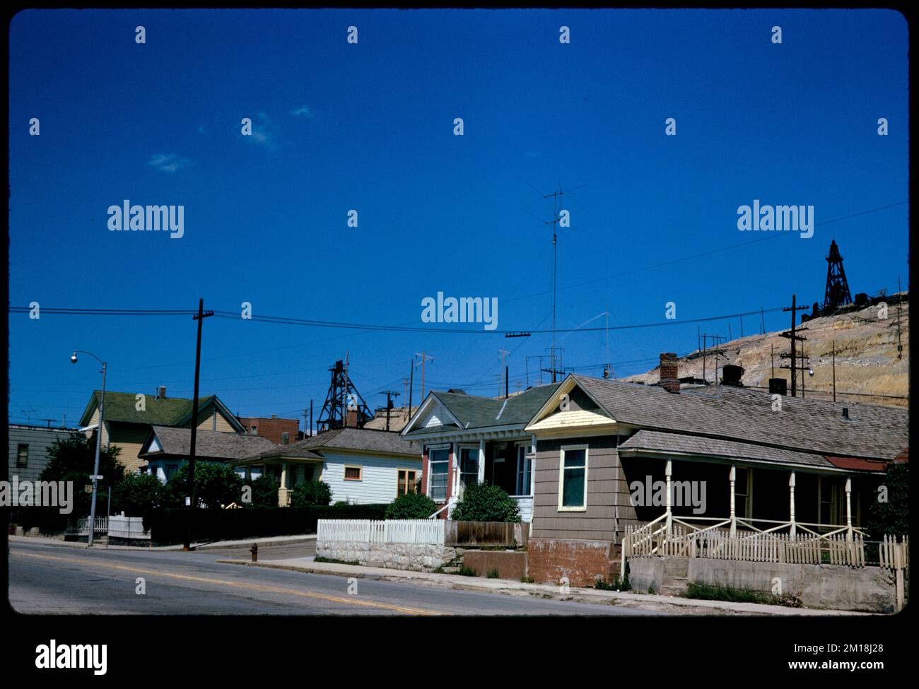 Street with houses in front of hill with mine head frames, Butte ...