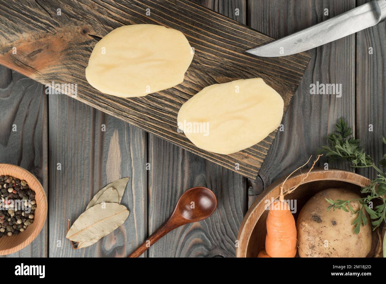 Cutting in half raw yellow potato with knife on kitchen wooden board ...