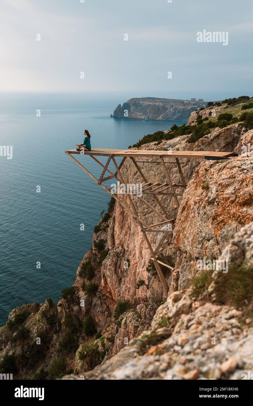 A girl sits on a wooden springboard for jumping with a rope. In a dark ...