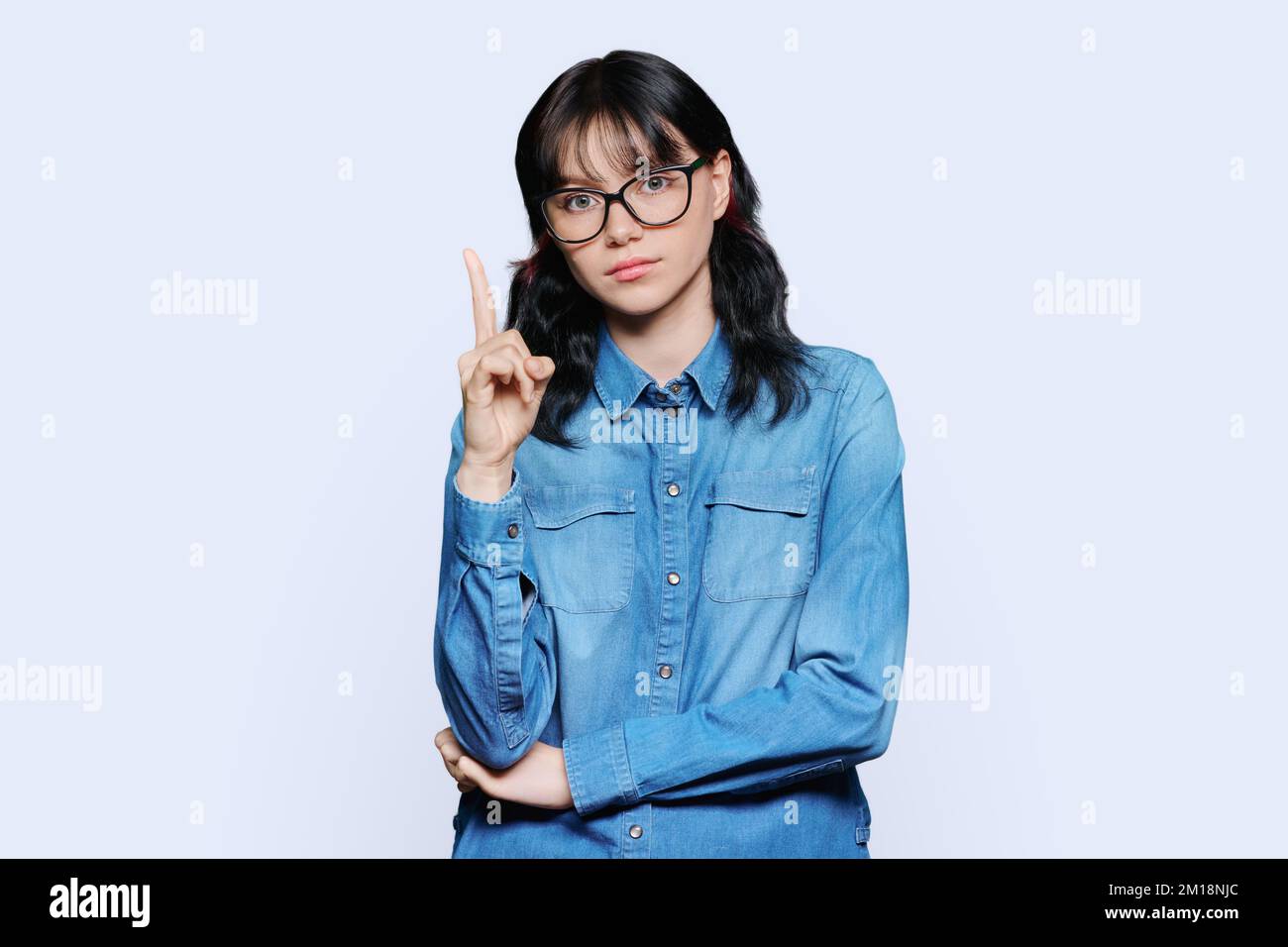 Serious young woman showing index finger up, over white studio ...