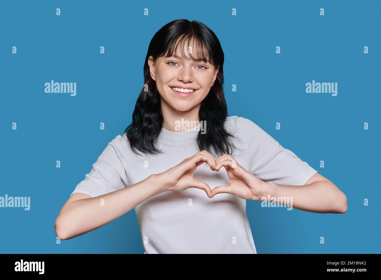 Smiling teenage female showing heart with hands on blue background ...