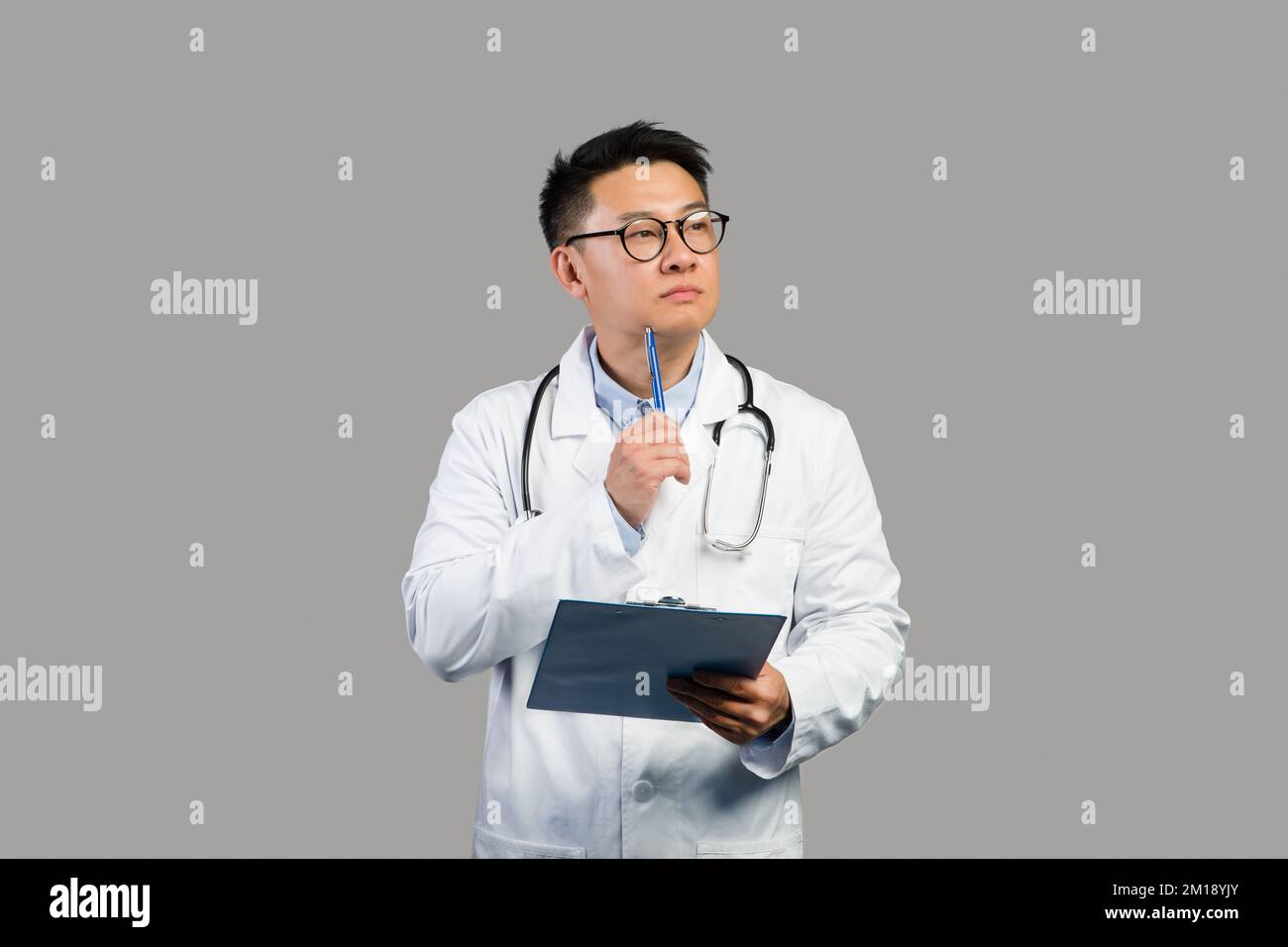 Pensive serious adult chinese male in white coat, glasses with tablet ...
