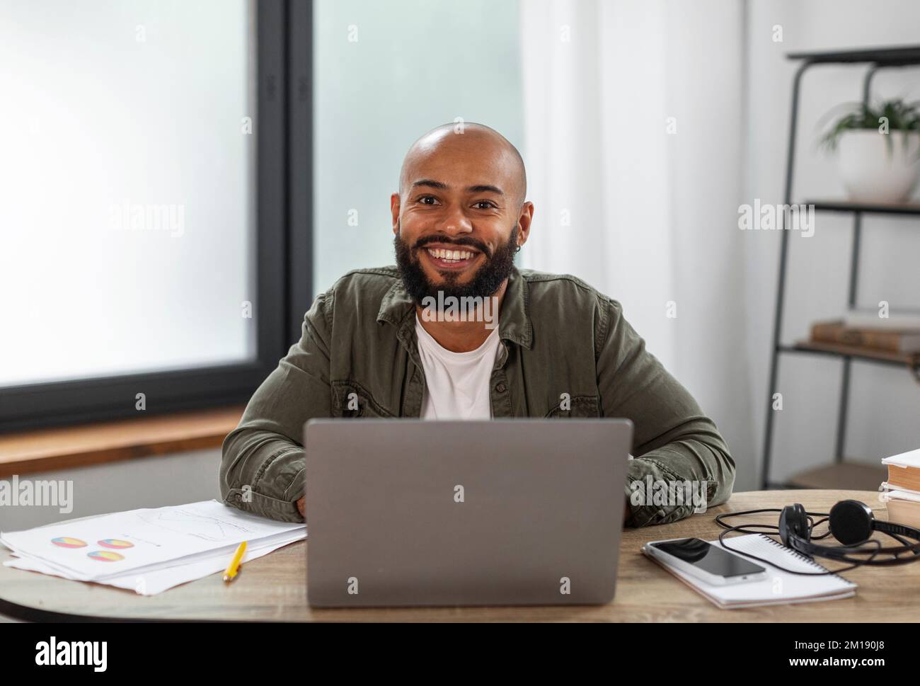 Portrait of happy latin male freelancer sitting at table, working on ...