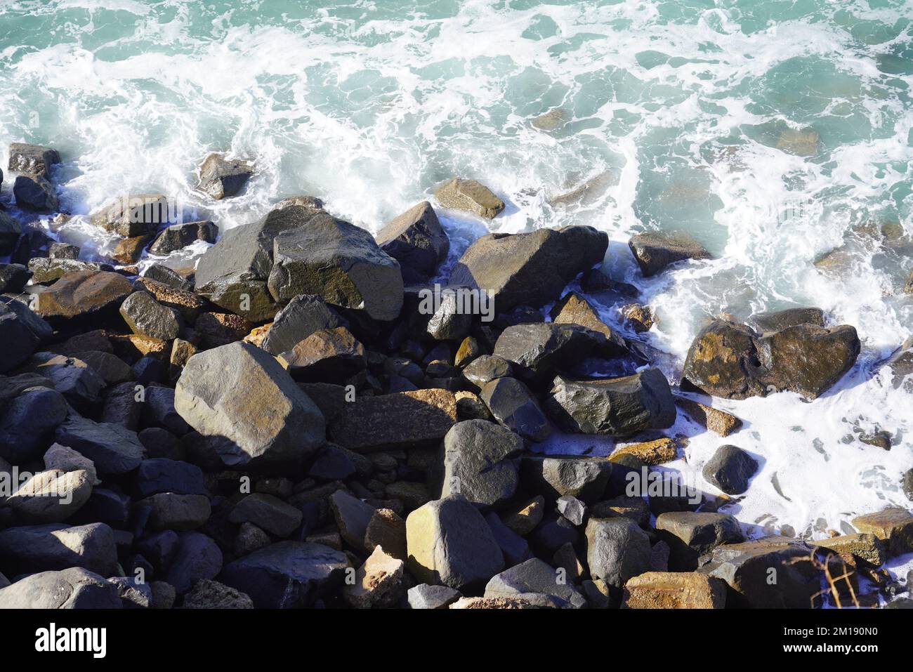 The small wet rocks on the beach with foamy waves crashing them in ...